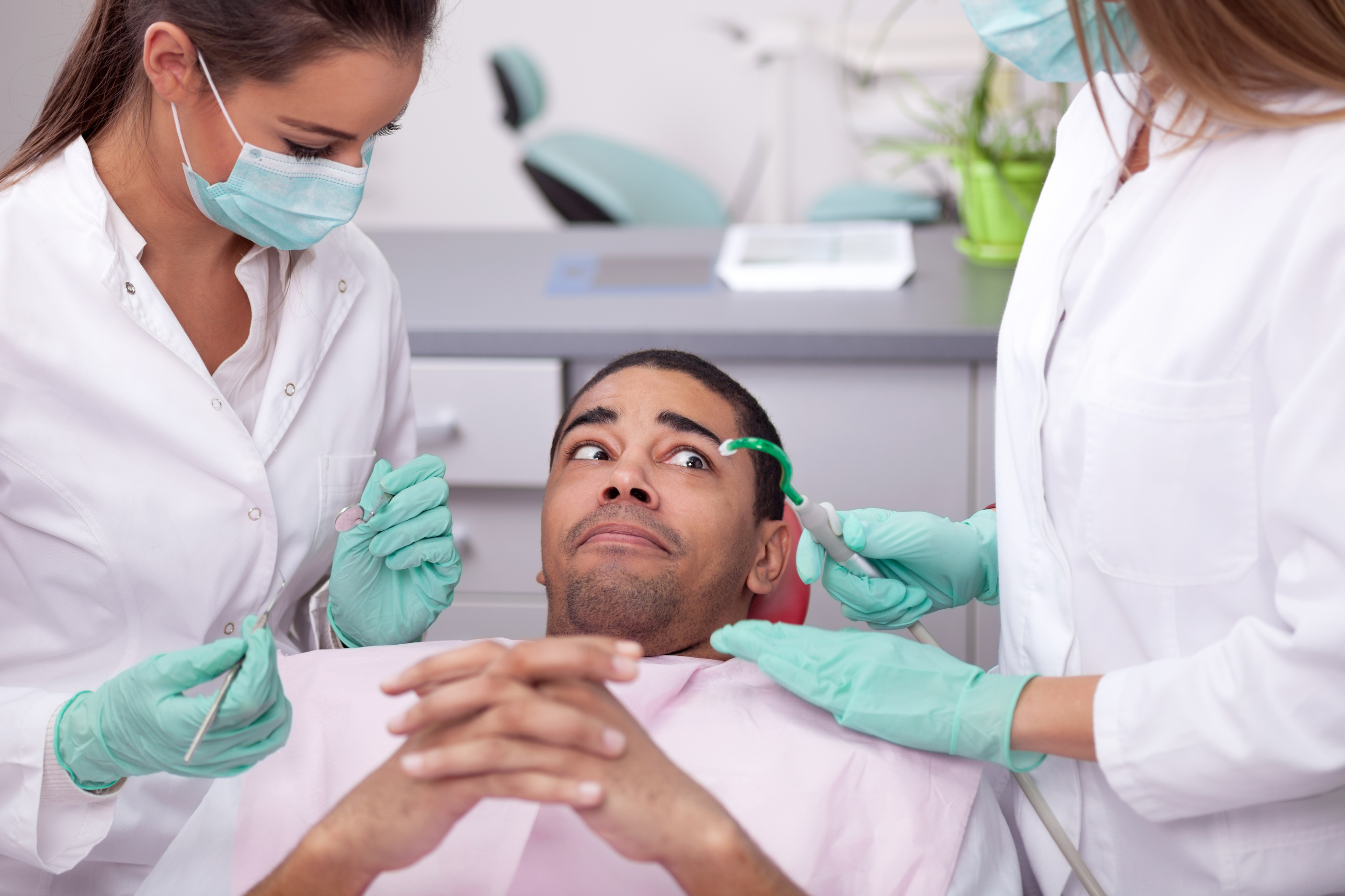 Scared man in dental chair with dentist and team members above him ...